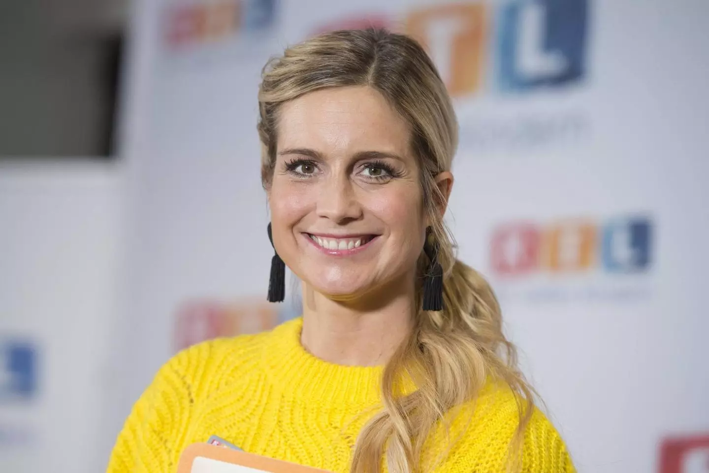 Susanna Ohlen: reporterka ima plavu kosu u pletenici, nosi žuti džemper i smiješi se u kameru
